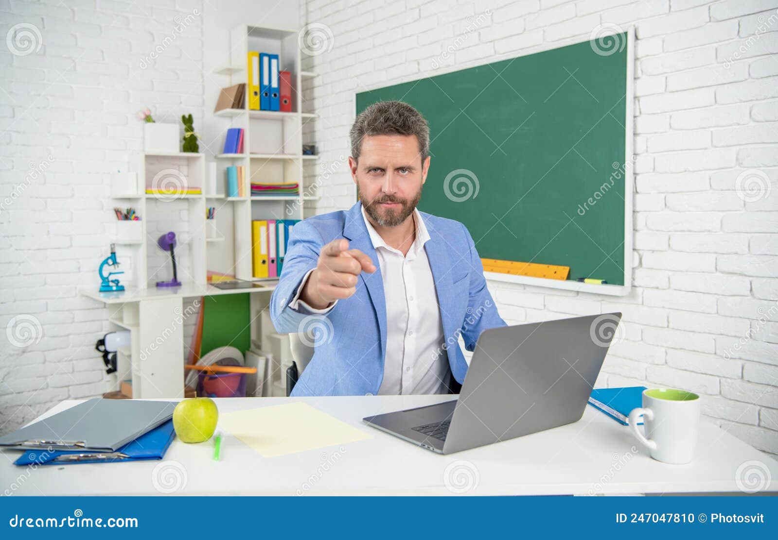 Serious School Teacher in Classroom with Computer at Blackboard. Point ...