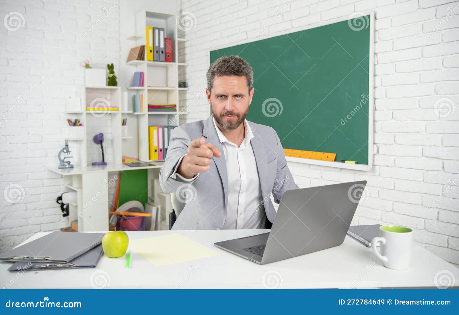 Serious School Teacher in Classroom with Computer at Blackboard. Point ...