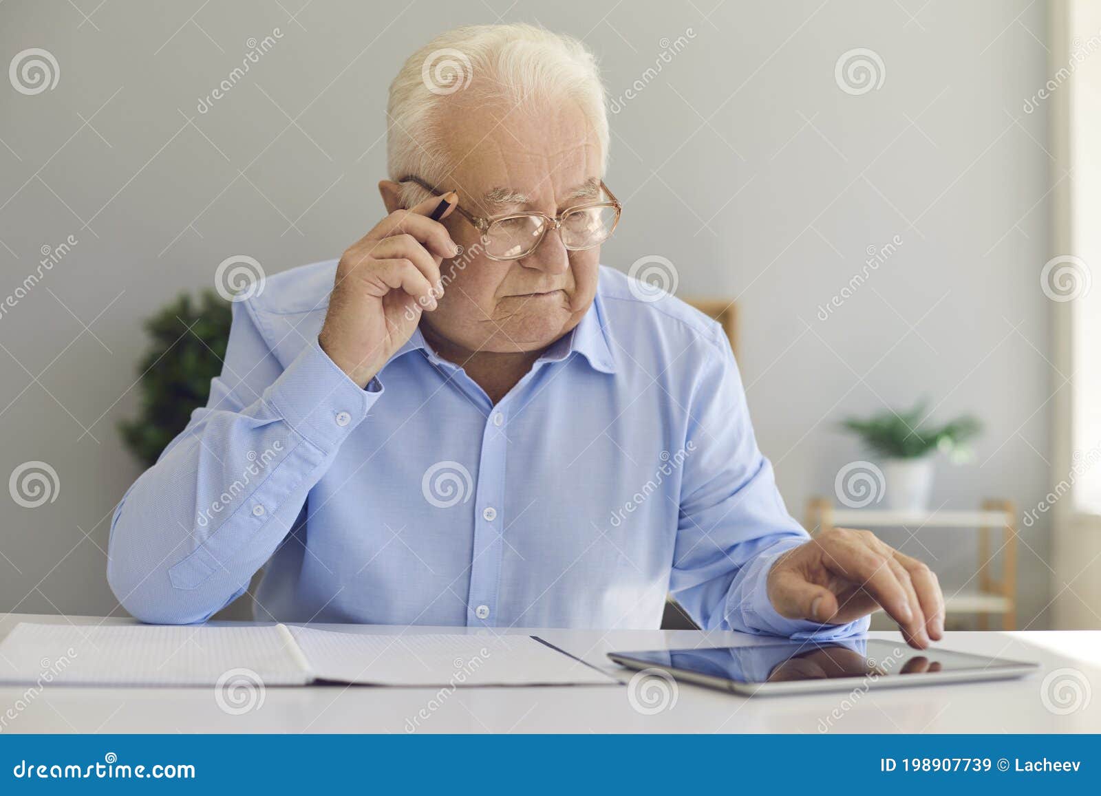 Serious Old Man Sitting at Desk at Home Using Tablet Computer and ...