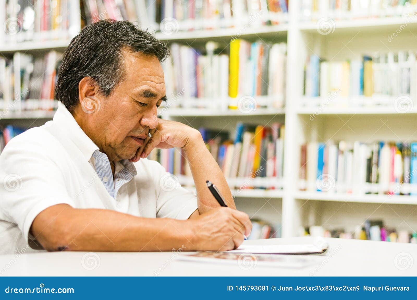 Serious Senior Man Sitting on a Library Bench, Writing in His Book ...