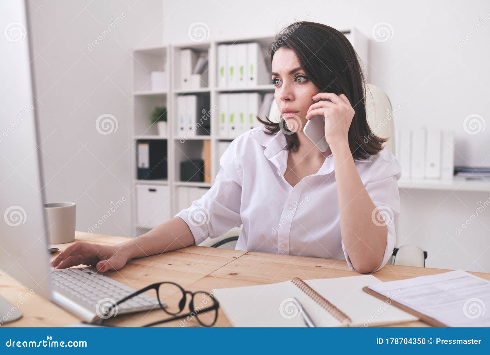 Serious Young Secretary or Office Manager Sitting by Desk in Front of ...