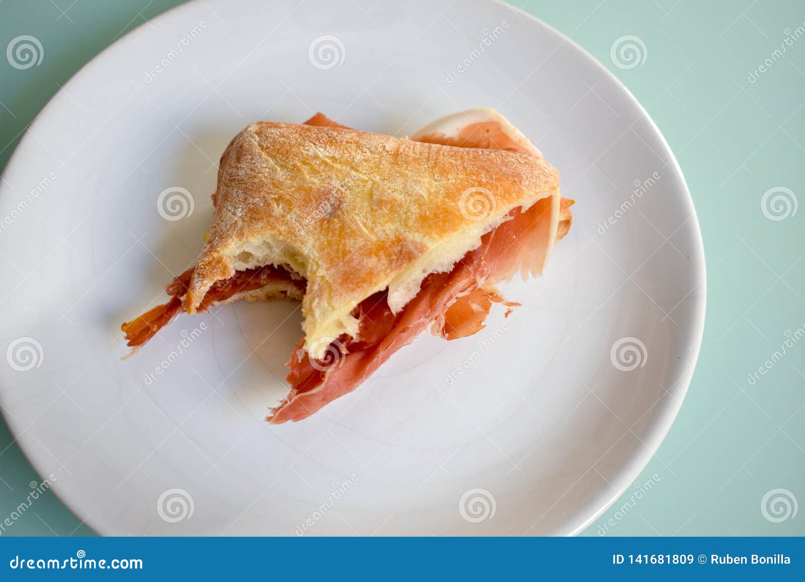 A Serrano Ham Sandwich with a Big Bite at a Corner on a White Plate on ...