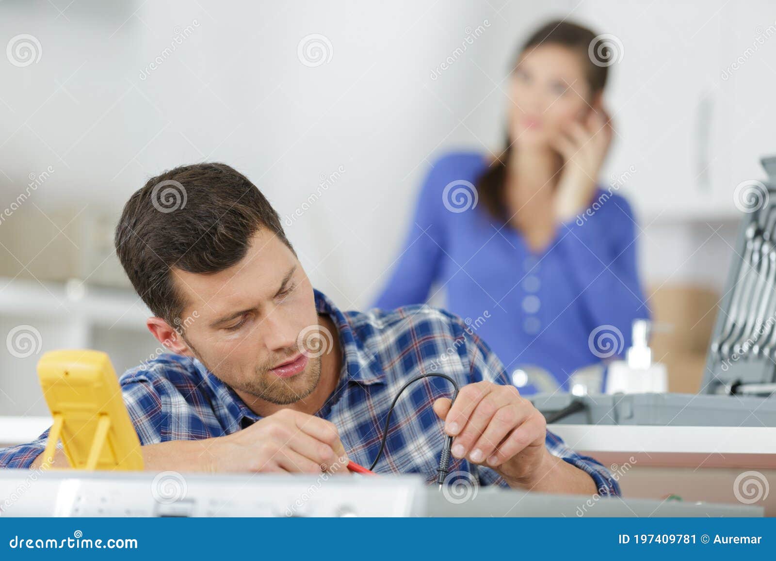 Serviceman Testing Appliance with Multimeter Housewife in Background ...