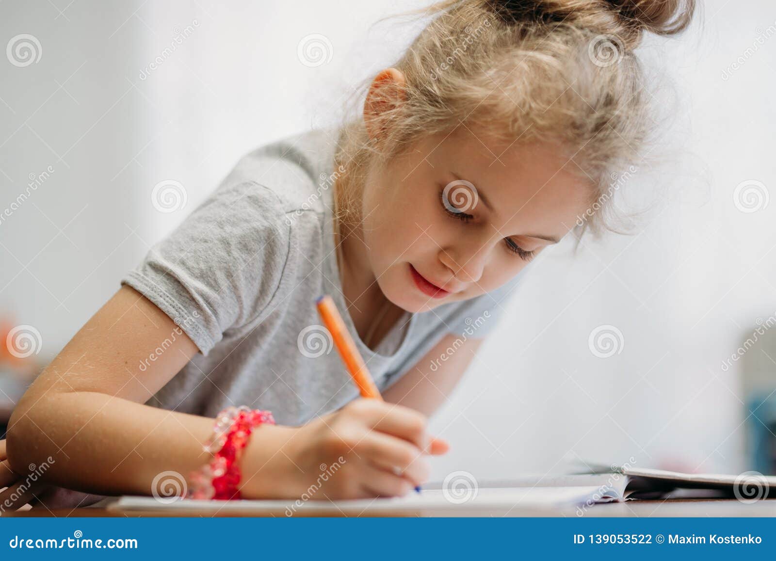 A Seven-year-old Girl Sits at Home at a Table and Writes in a Notebook ...