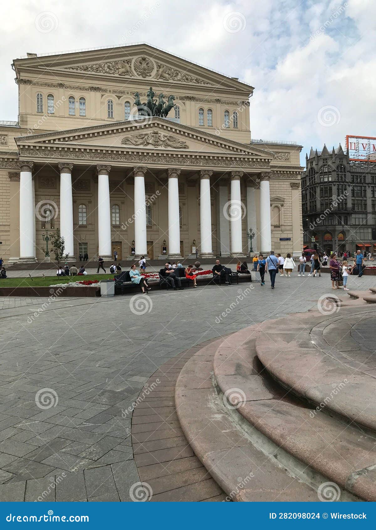 Several People Walking Around Outside a Big Building with Pillars and ...