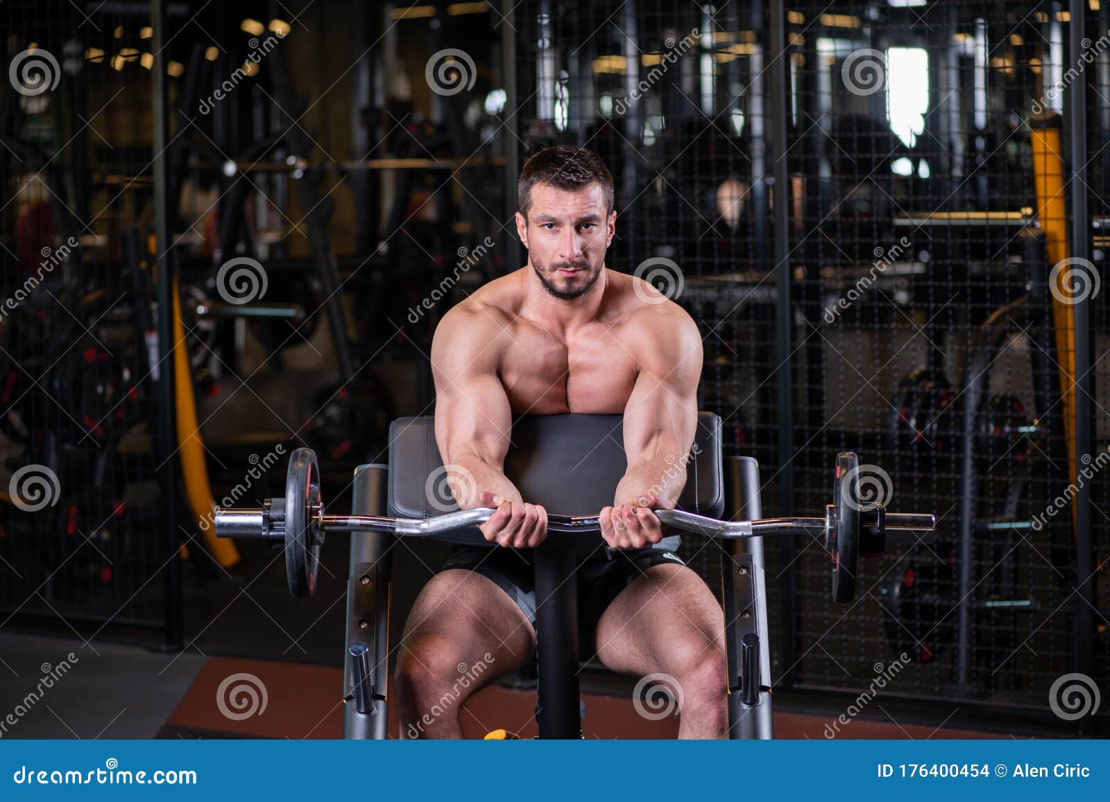 Muscular Man Sitting on the Bench and Doind Biceps Exercise. Front View ...