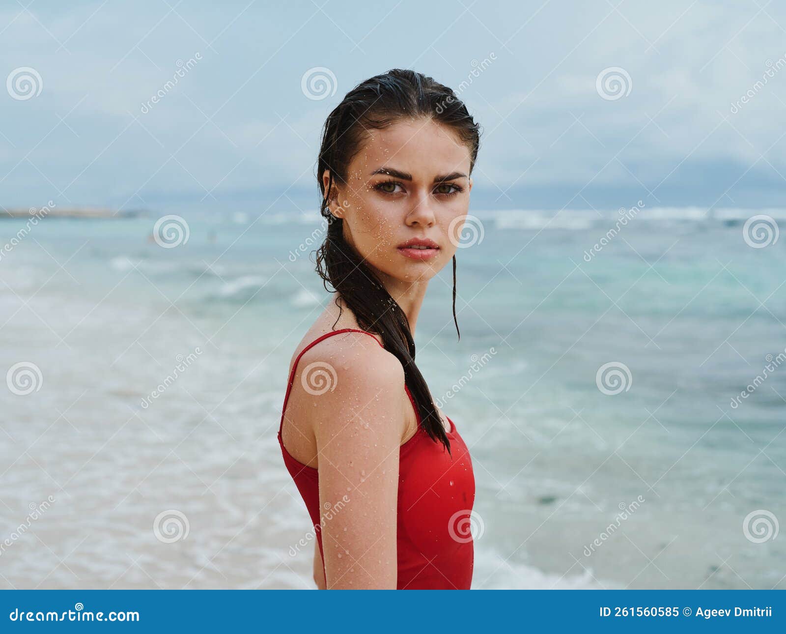 Woman In Red Swimsuit On Ocean Beach With Wet Hair Looking At Camera Slim Pumped Body Sunscreen
