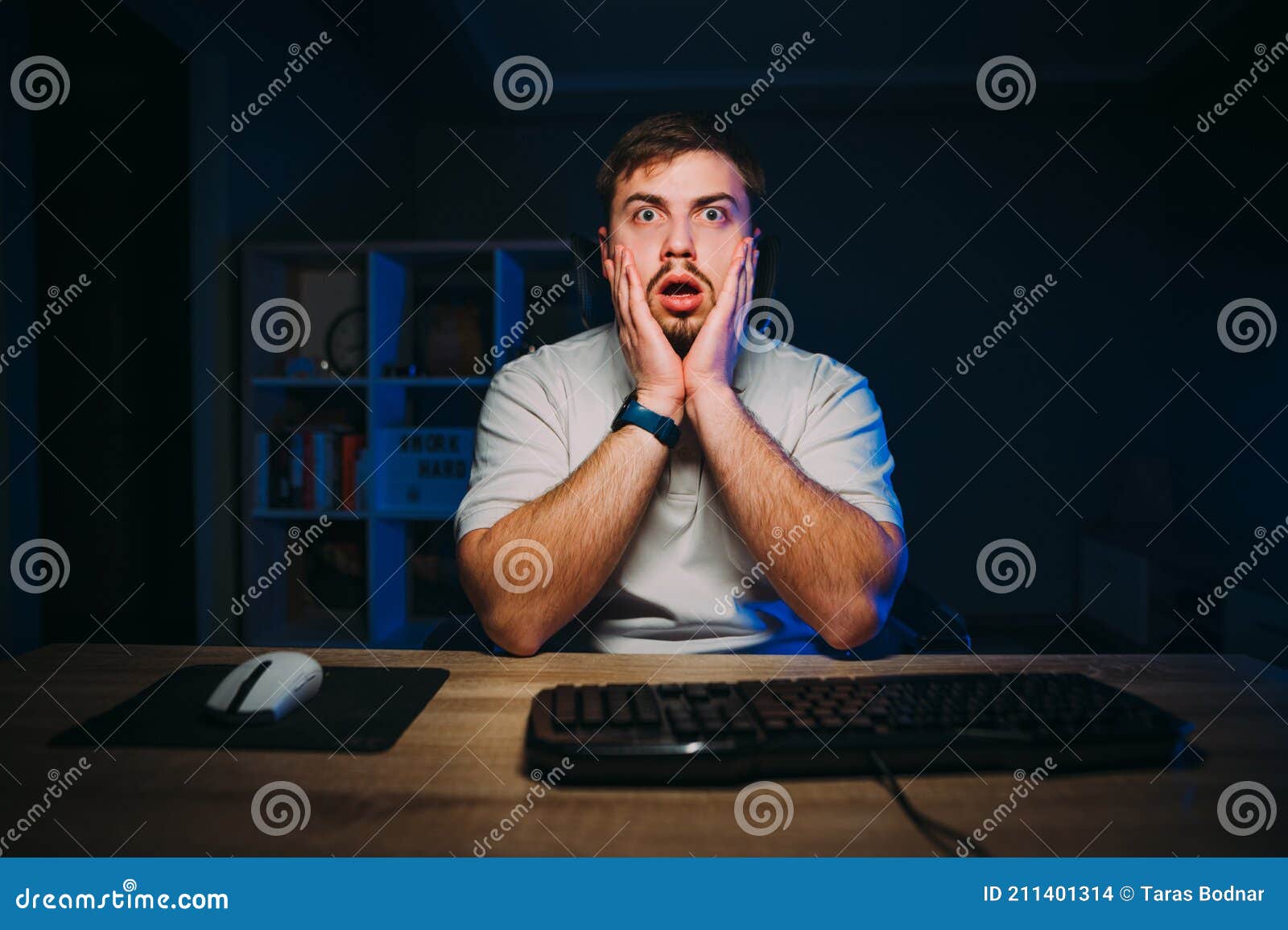 Shocked Freelancer with a Beard Uses a Computer at Night in the Bedroom ...