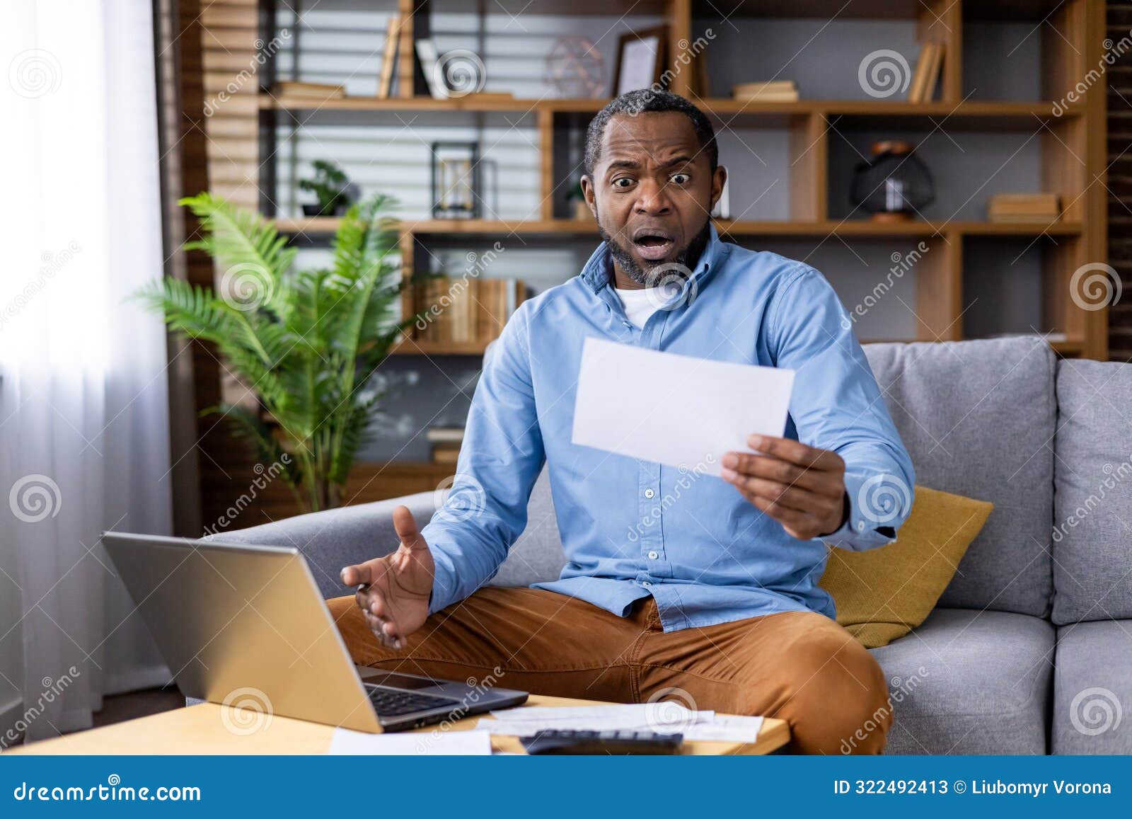 Shocked Man Looking at Document while Working on Laptop at Home Stock ...
