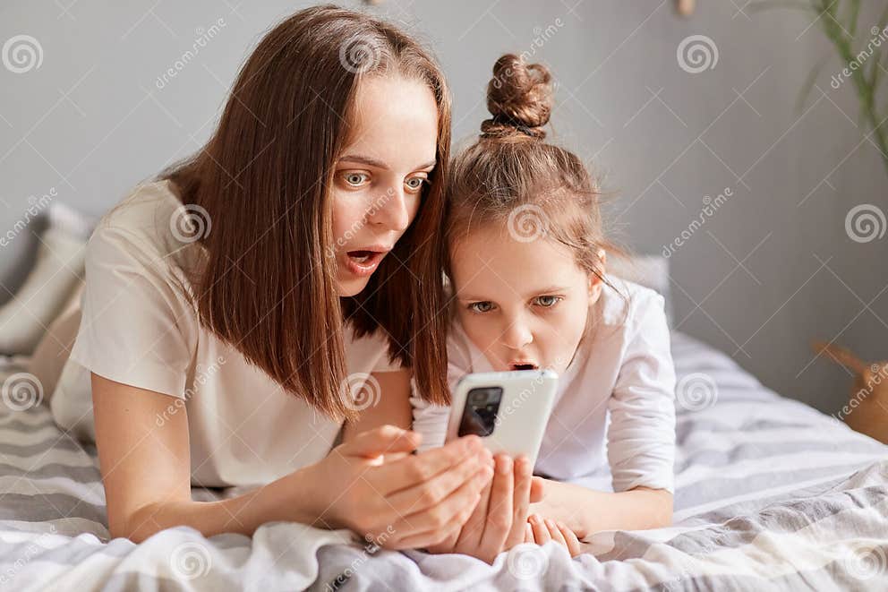 Shocked Surprised Mother And Daughter Using Mobile Phone Laying On Bed