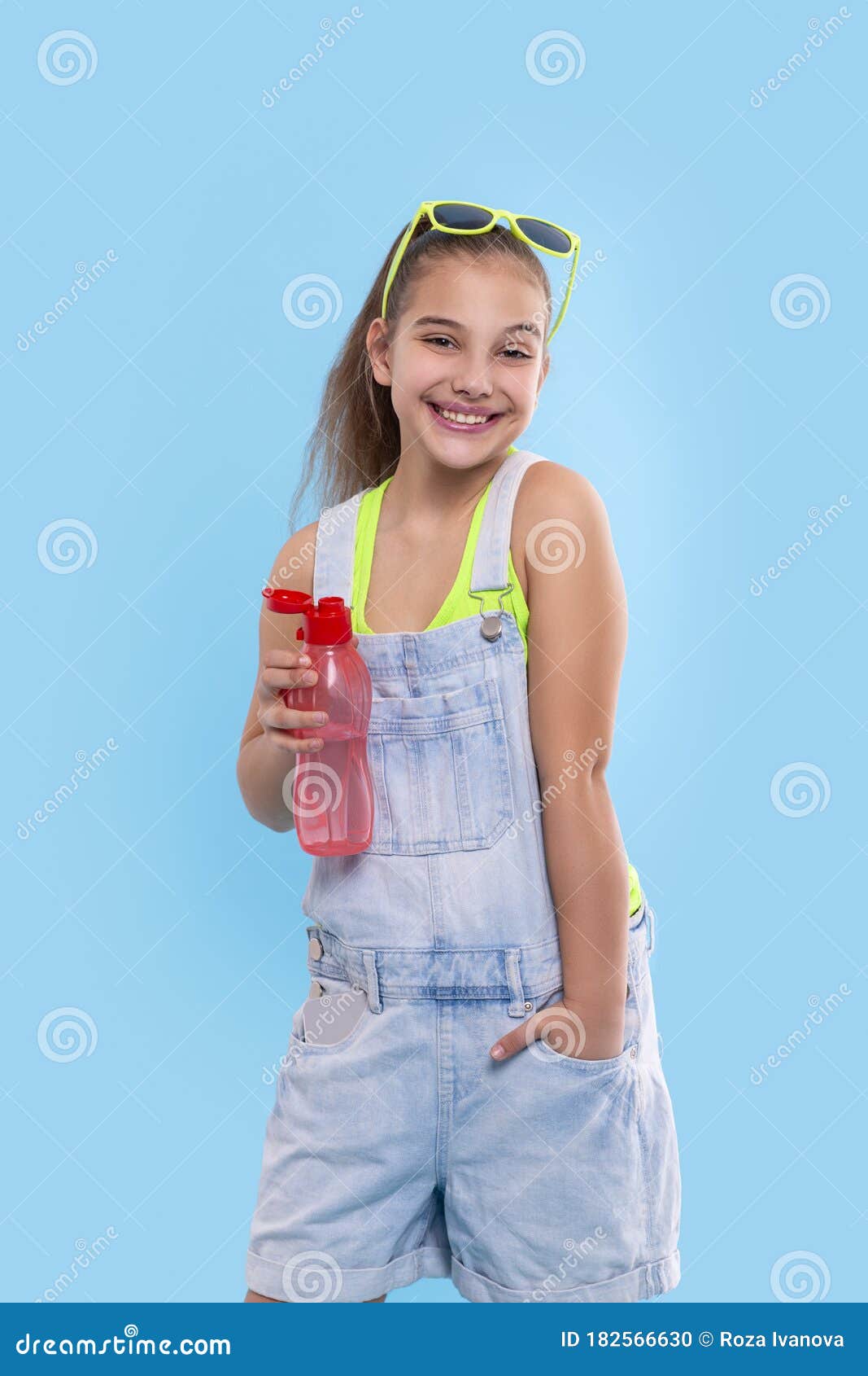 A Young Brunette Girl Wearing Denim Overalls Shorts Stands With A Red