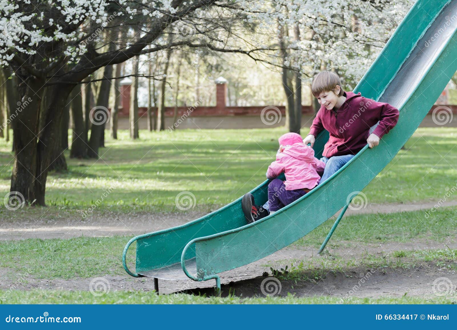 Sibling Children Sliding Down On Old Park Playground Slide At Blooming ...