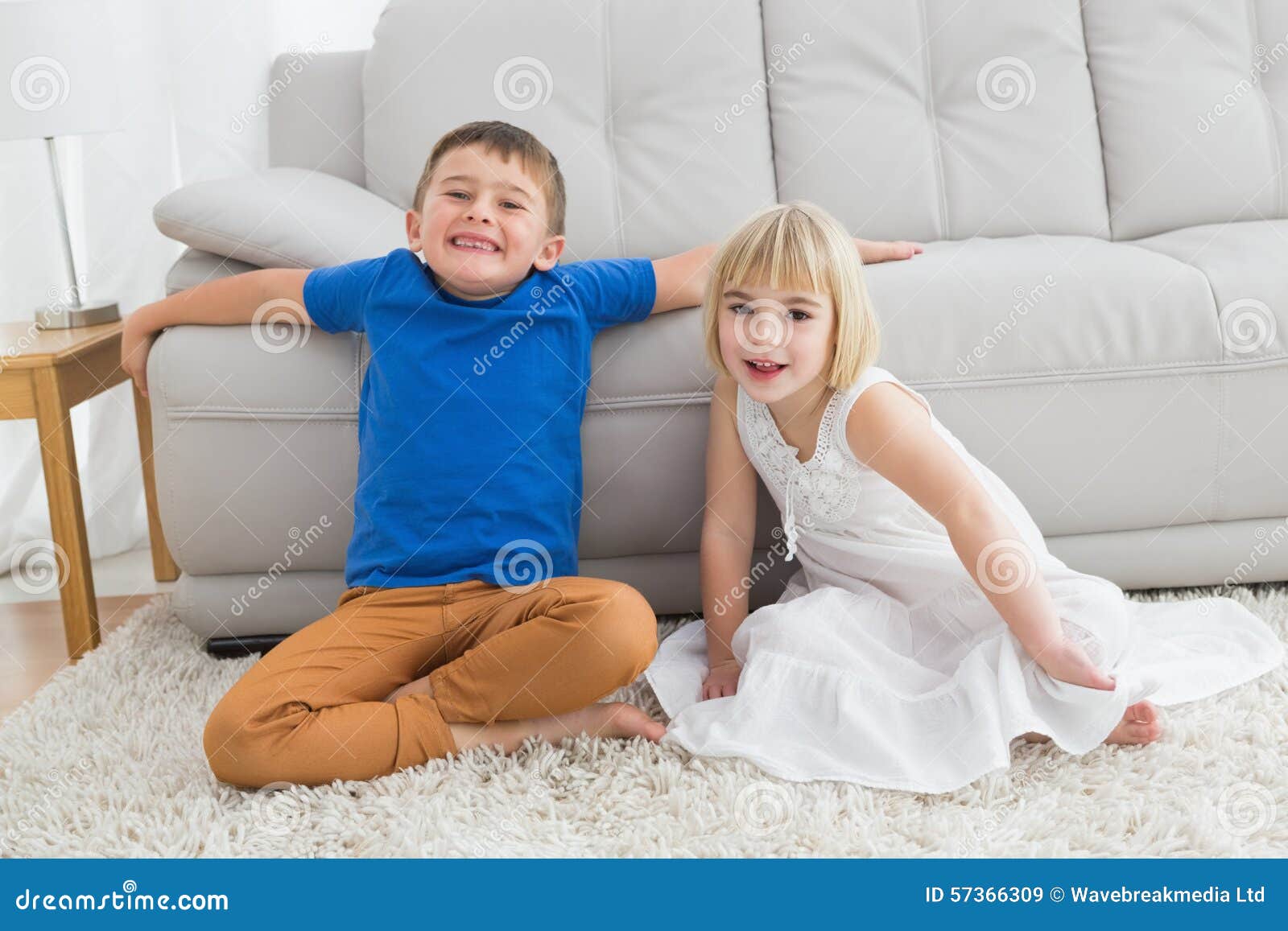 Siblings Sitting On The Floor And Smiling At Camera Together Stock