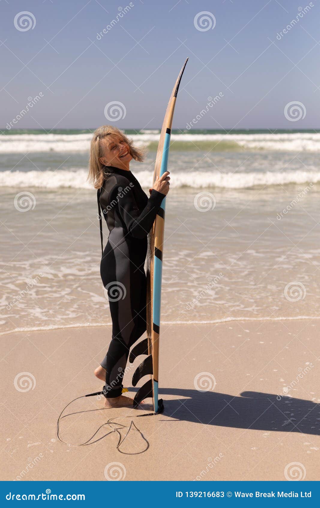Side View of Senior Female Surfer Standing with Surfboard on the Beach ...