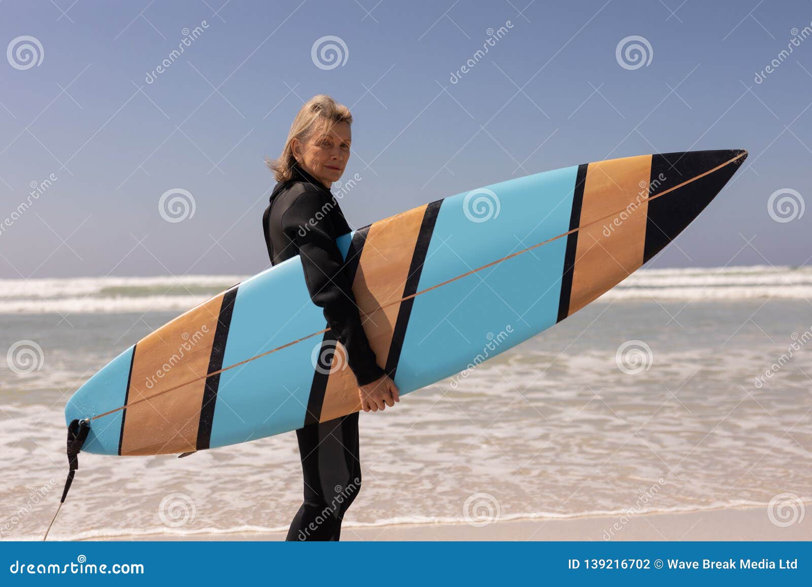 Side View of Senior Female Surfer Standing with Surfboard on the Beach ...
