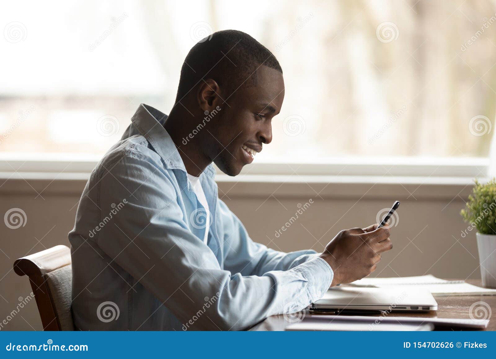 Side View African Guy Sit at Table Smiling Using Smartphone Stock Photo ...