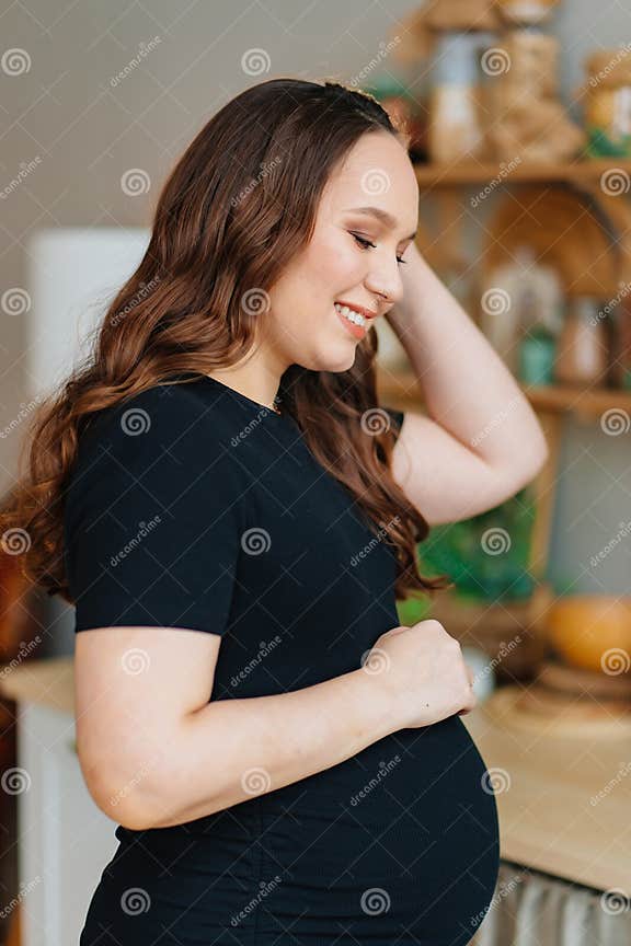 Side View Pregnant Woman In Black Dress Touches Stomach In Home