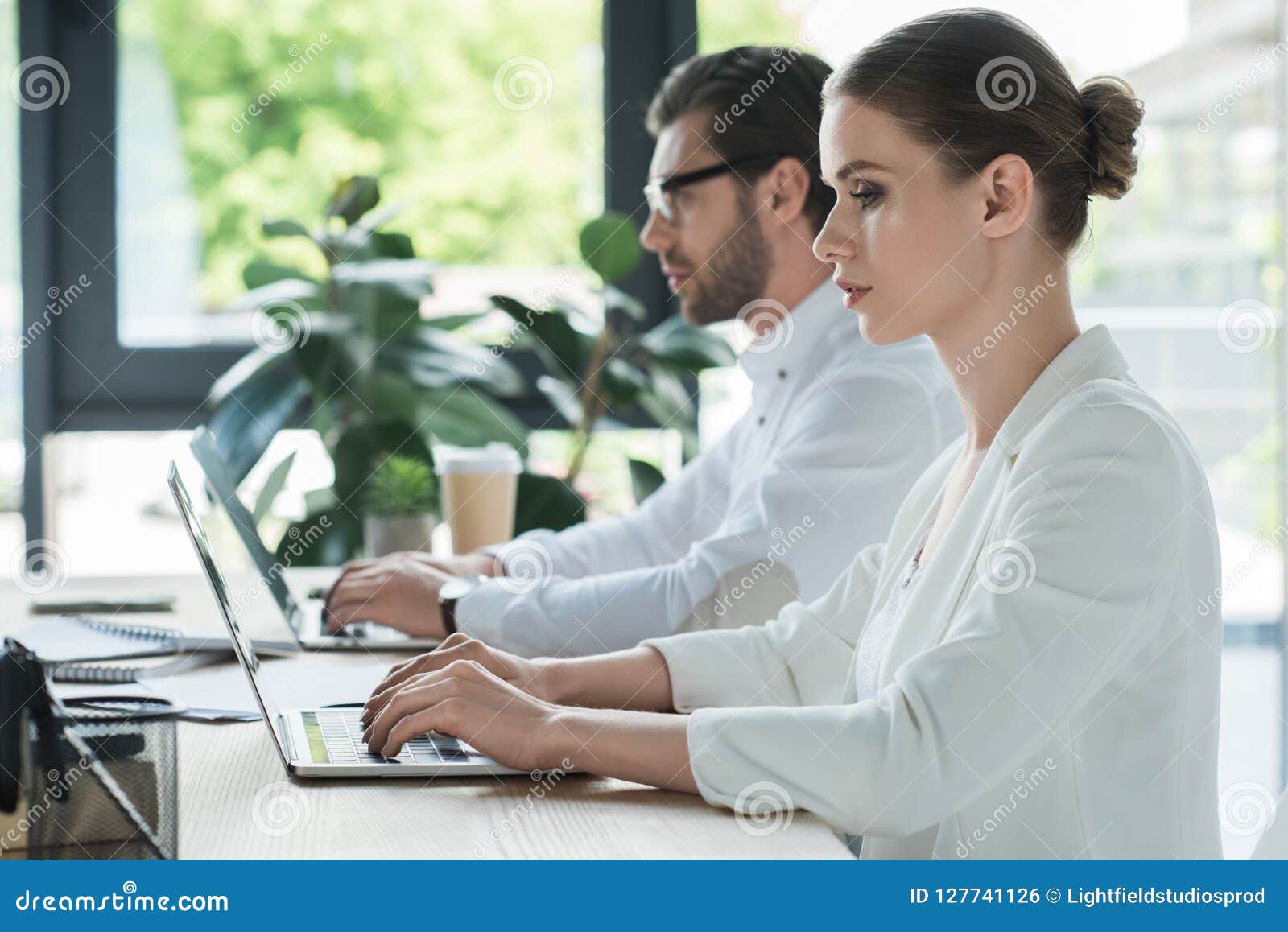 Side View of Concentrated Young Managers Working with Laptops Together ...