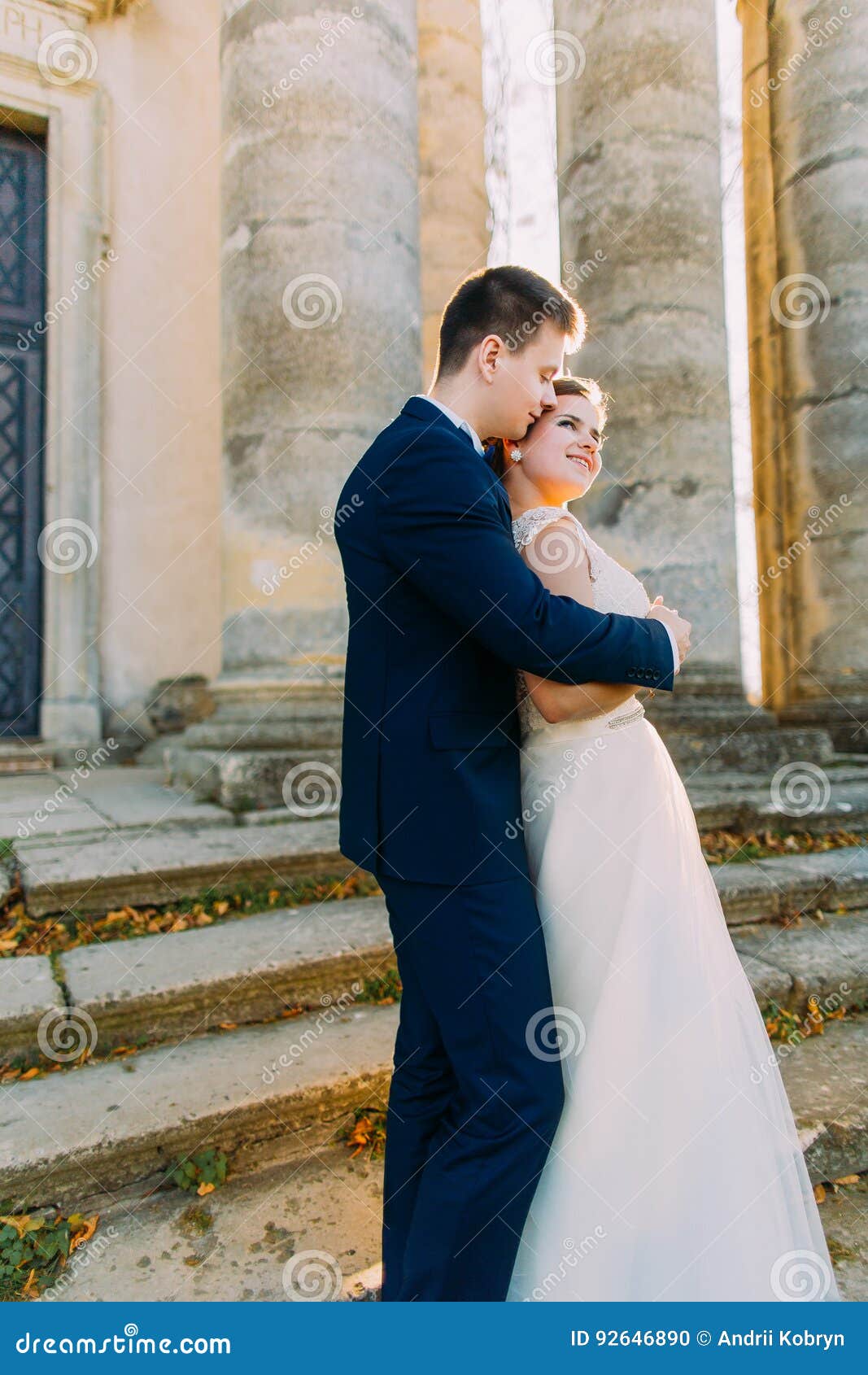 The Side View Of The Groom Hugging The Bride Back While Standing On The ...