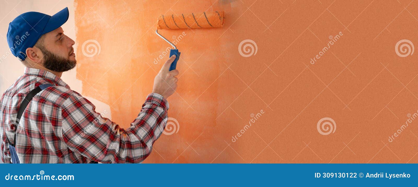 Side View of Handsome Young Painter in Blue Cap Painting a Wall with ...