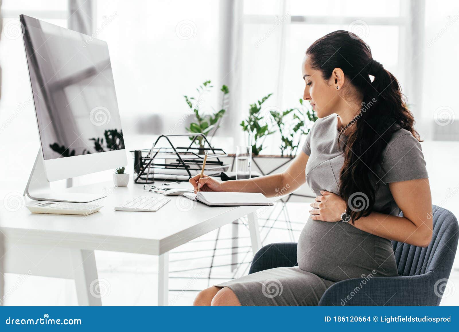 View of Pregnant Woman Sitting Behind Table with Computer, Keyboard and ...