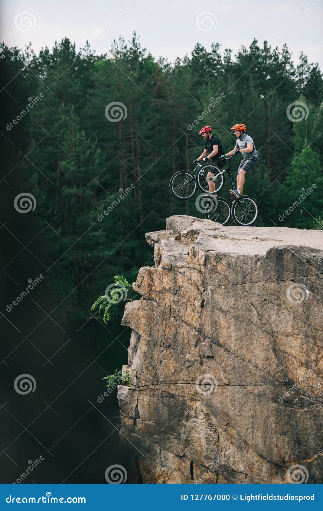 Side View of Trial Bikers Standing on Back Wheels on Rocky Cliff with ...