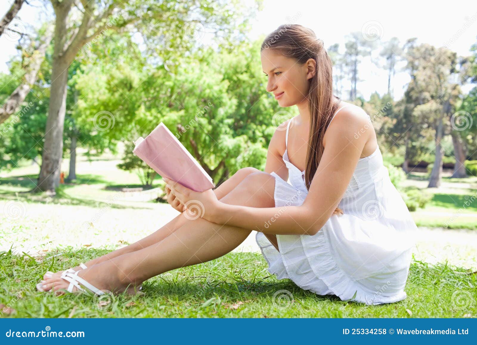 Side View Of A Woman Sitting On The Lawn While Reading A Book Royalty