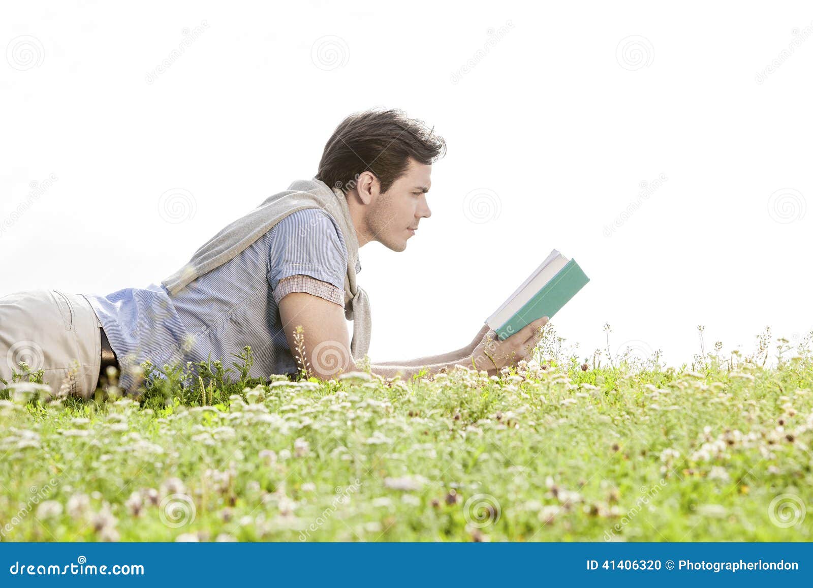 Side View of Young Man Reading Book while Lying on Grass Against Clear ...