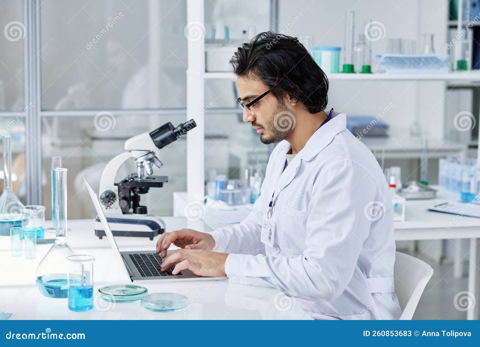Side View of Young Serious Laboratory Worker in Labcoat Sitting in ...