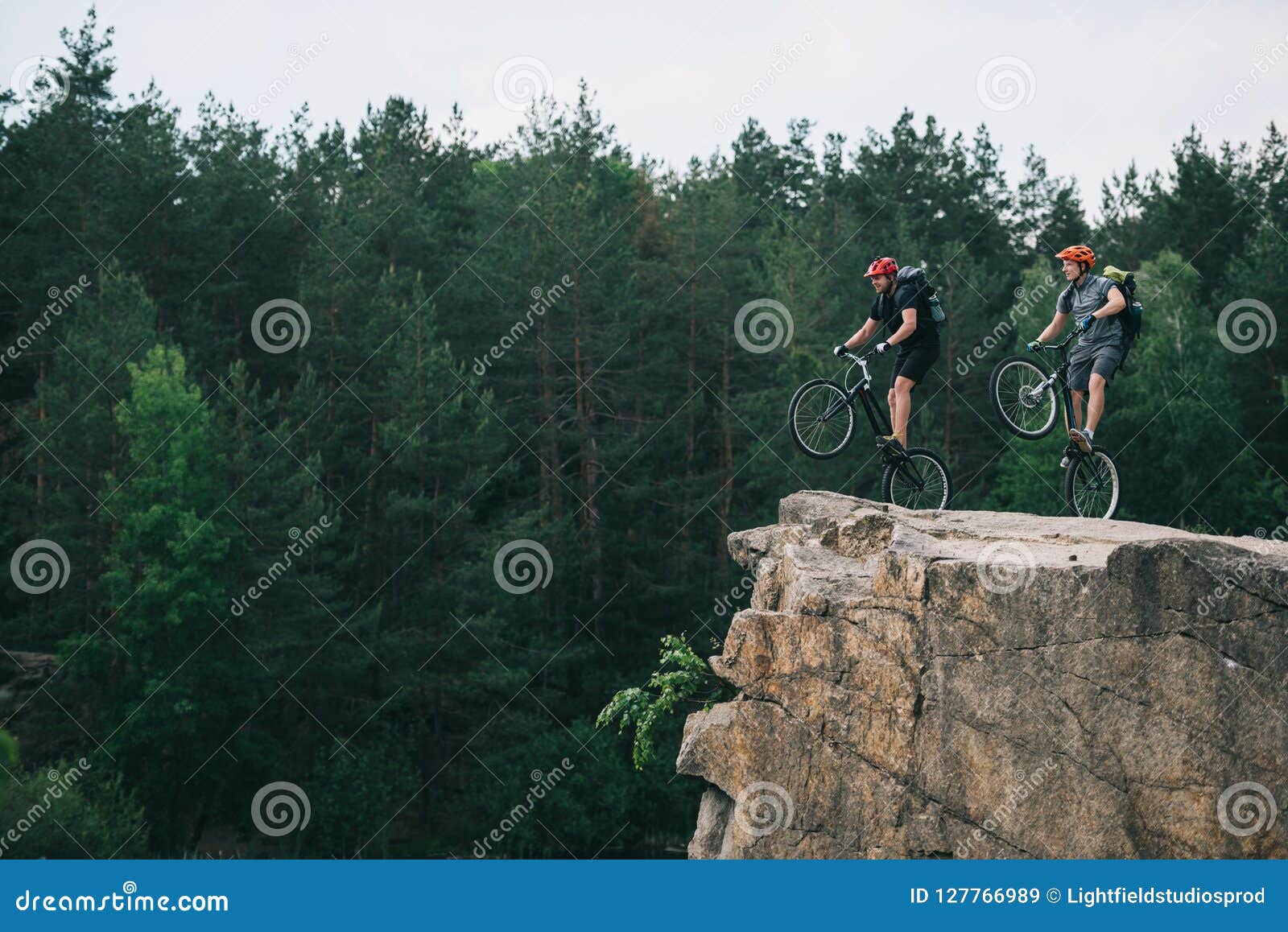 Side View of Young Trial Bikers with Backpacks Standing on Back Wheels ...