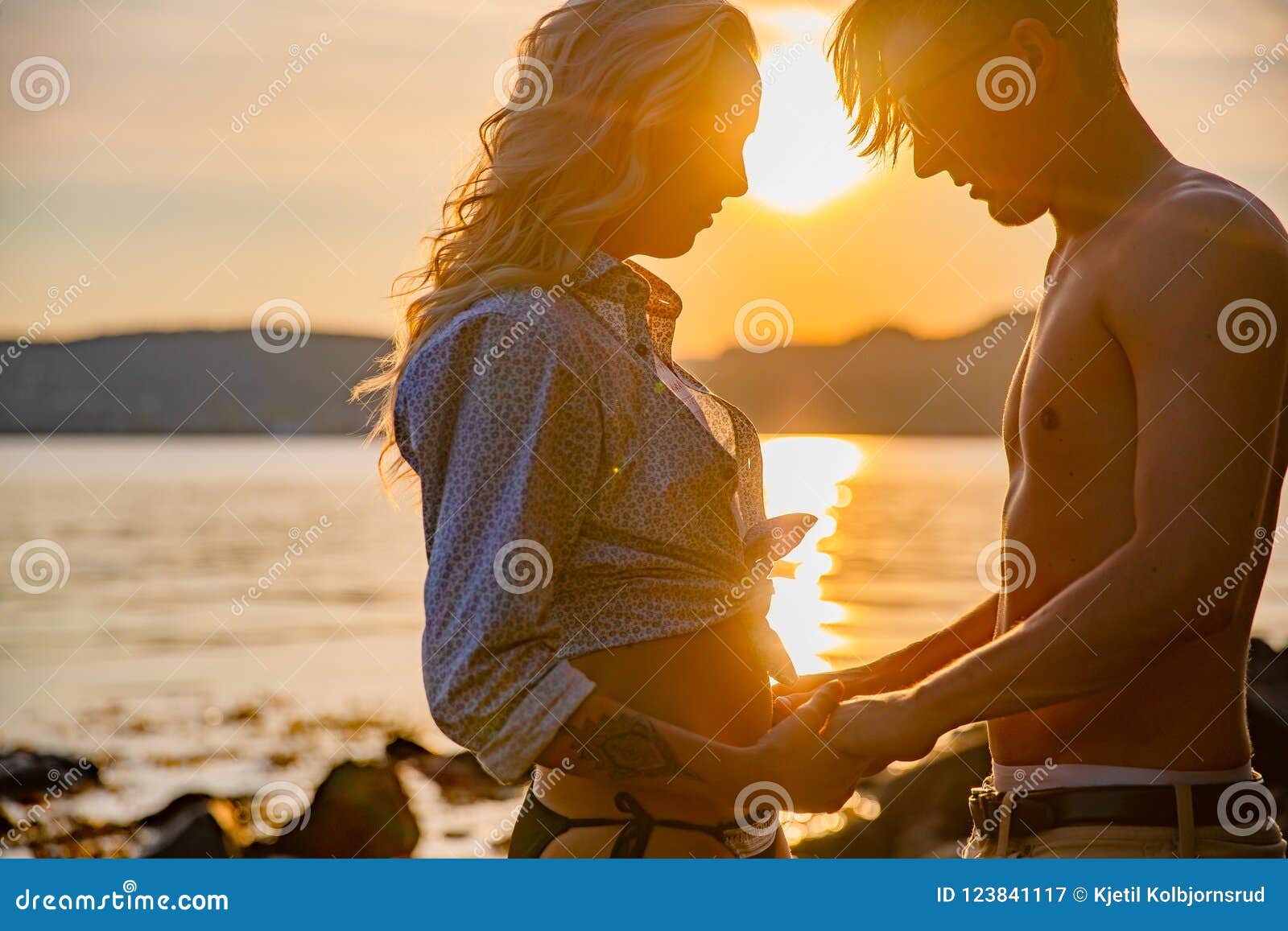 Silhouette Of Couple In Love Embracing At The Beach Against Sun Stock