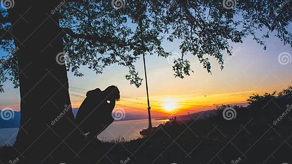 Silhouette of a Man Crouching Under a Tree during a Dramatic Sunset ...