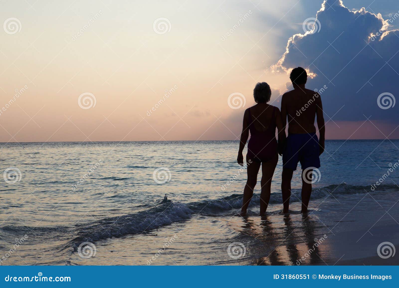 Silhouette Of Senior Couple Walking Along Beach At Sunset Stock Image