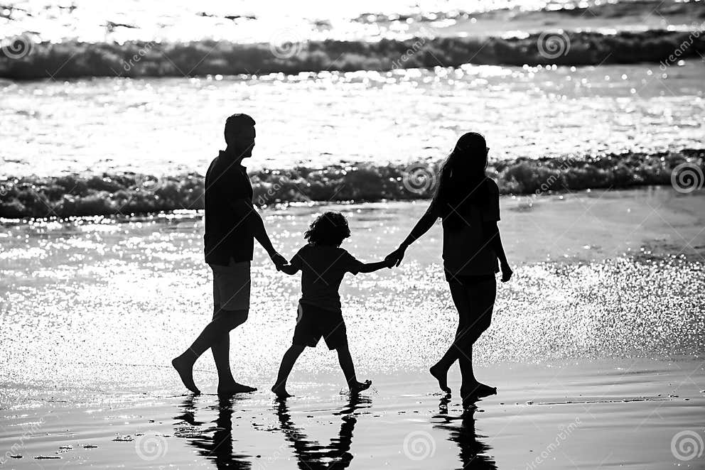 Silueta De Padre Madre E Hijo Agarrados De La Mano Y Caminando Por La Playa Foto De Archivo