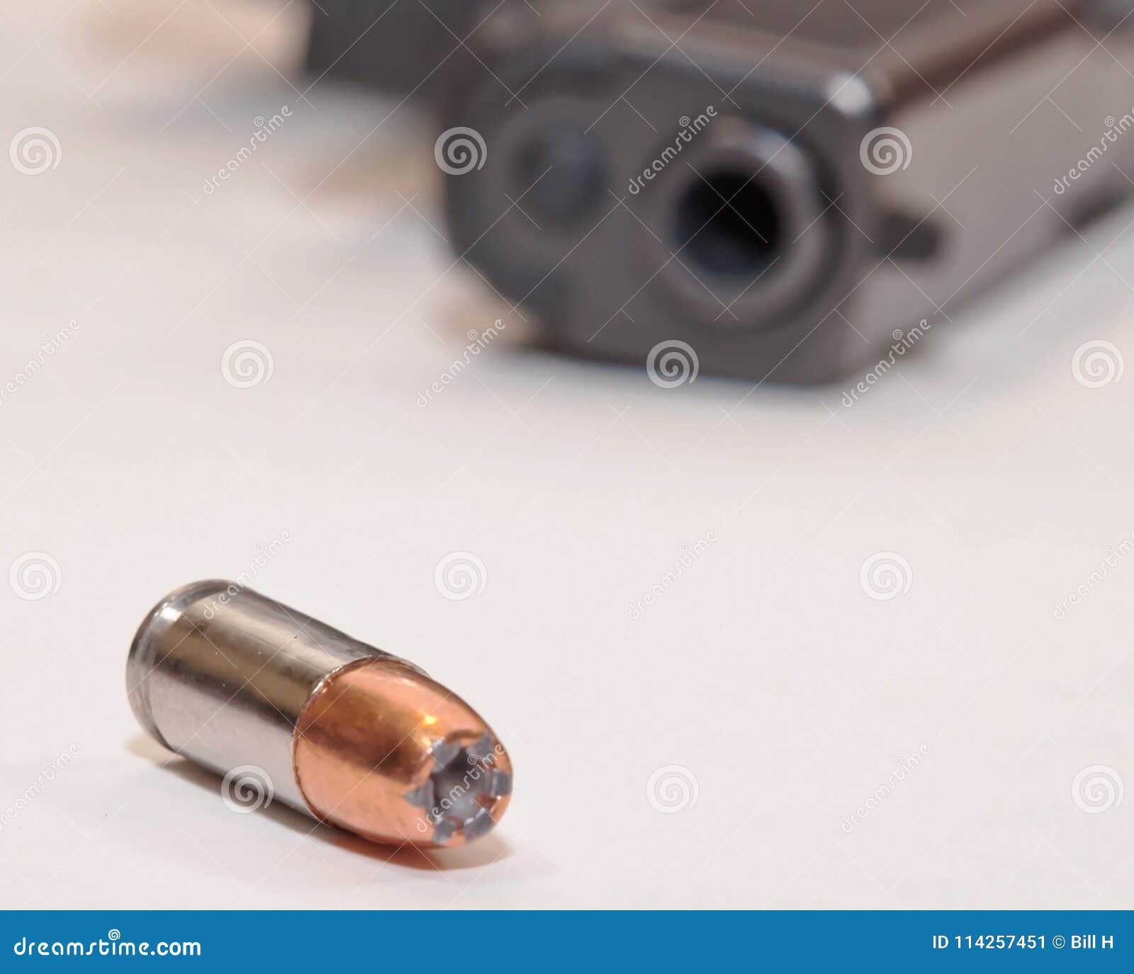 A Single Bullet on a White Table with a Black Pistol in the Background ...