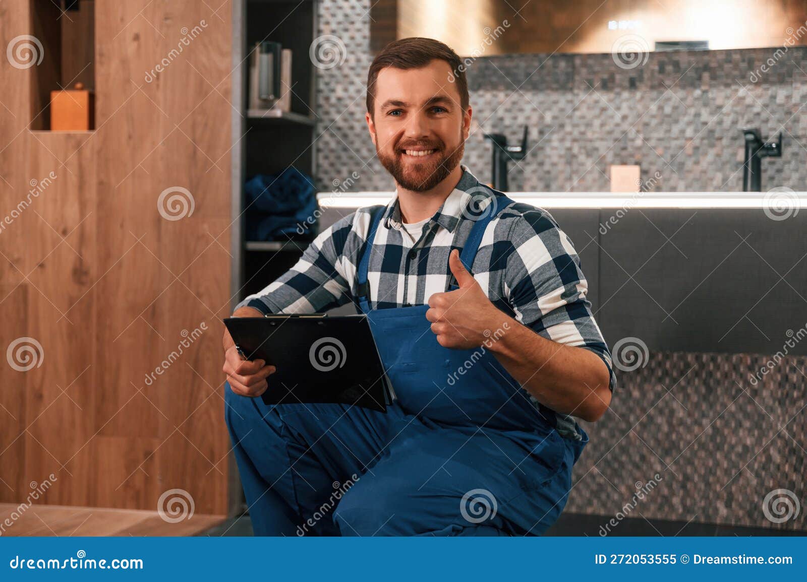 Sitting on the Floor with Notepad in Hands. Plumber in Blue Uniform is ...