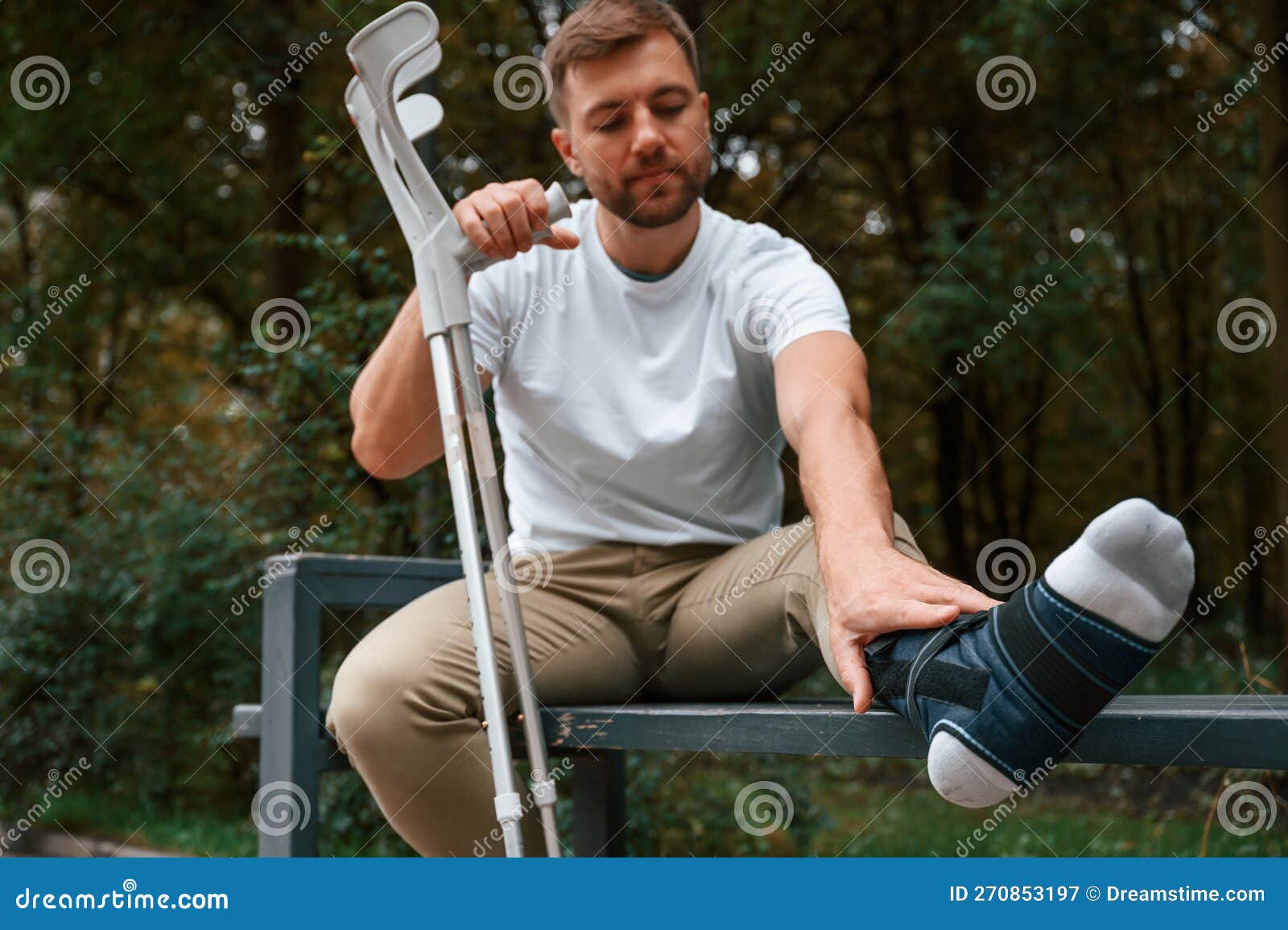 Sitting, Touching the Leg. Man with Crutches is in the Park Outdoors ...