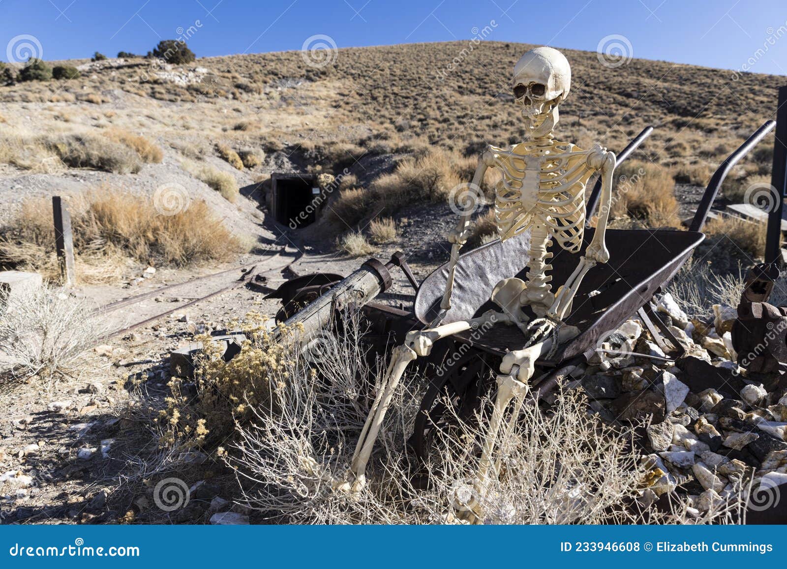 Skeleton Sitting in a Rusty Wheelbarrow Near a Min Opening in a Hill ...