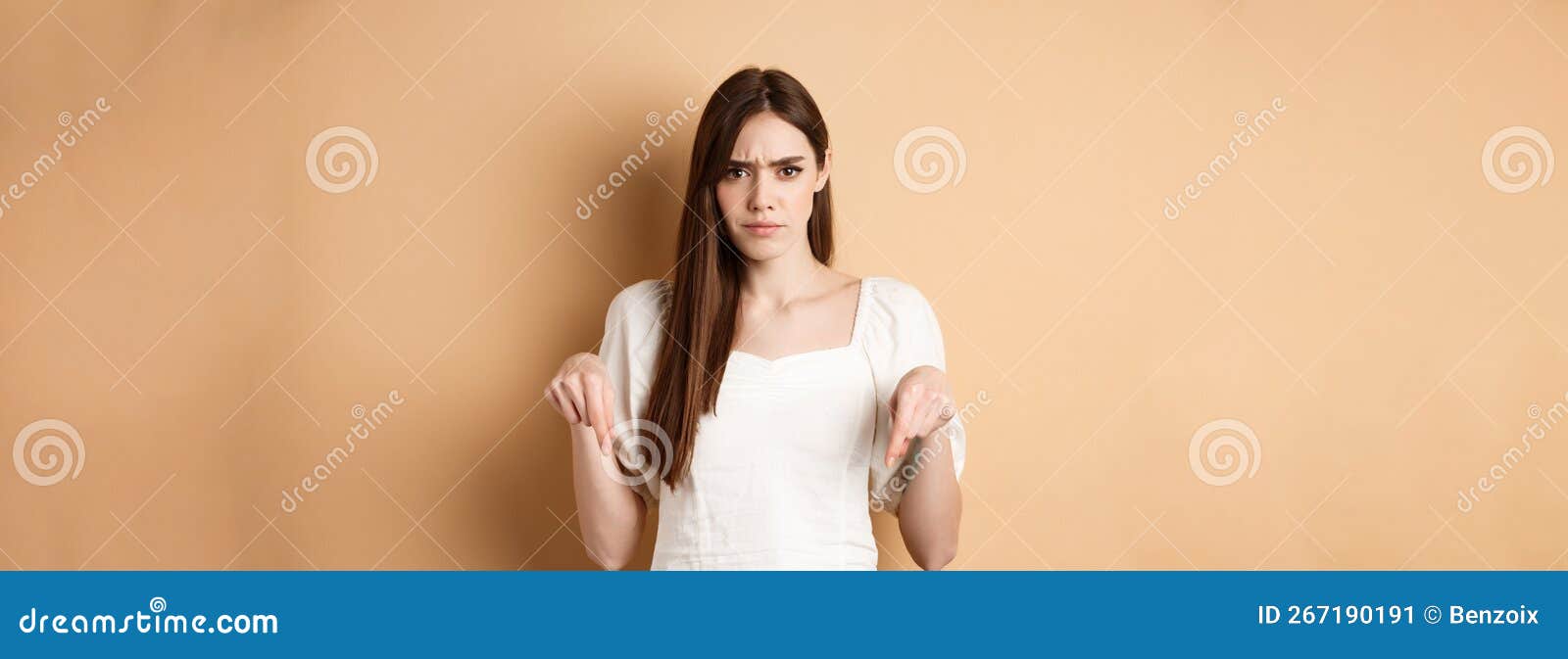 Skeptical Young Woman Frowning, Pointing Hands Down at Something Bad or ... Skeptical Young Woman Frowning, Pointing Hands Down at Something Bad or ...