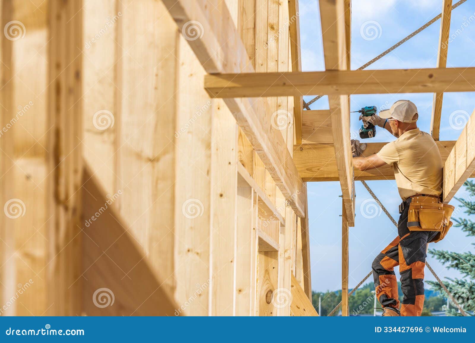 A Carpenter Works on a Wooden Framework of a House Under a Clear Blue ...