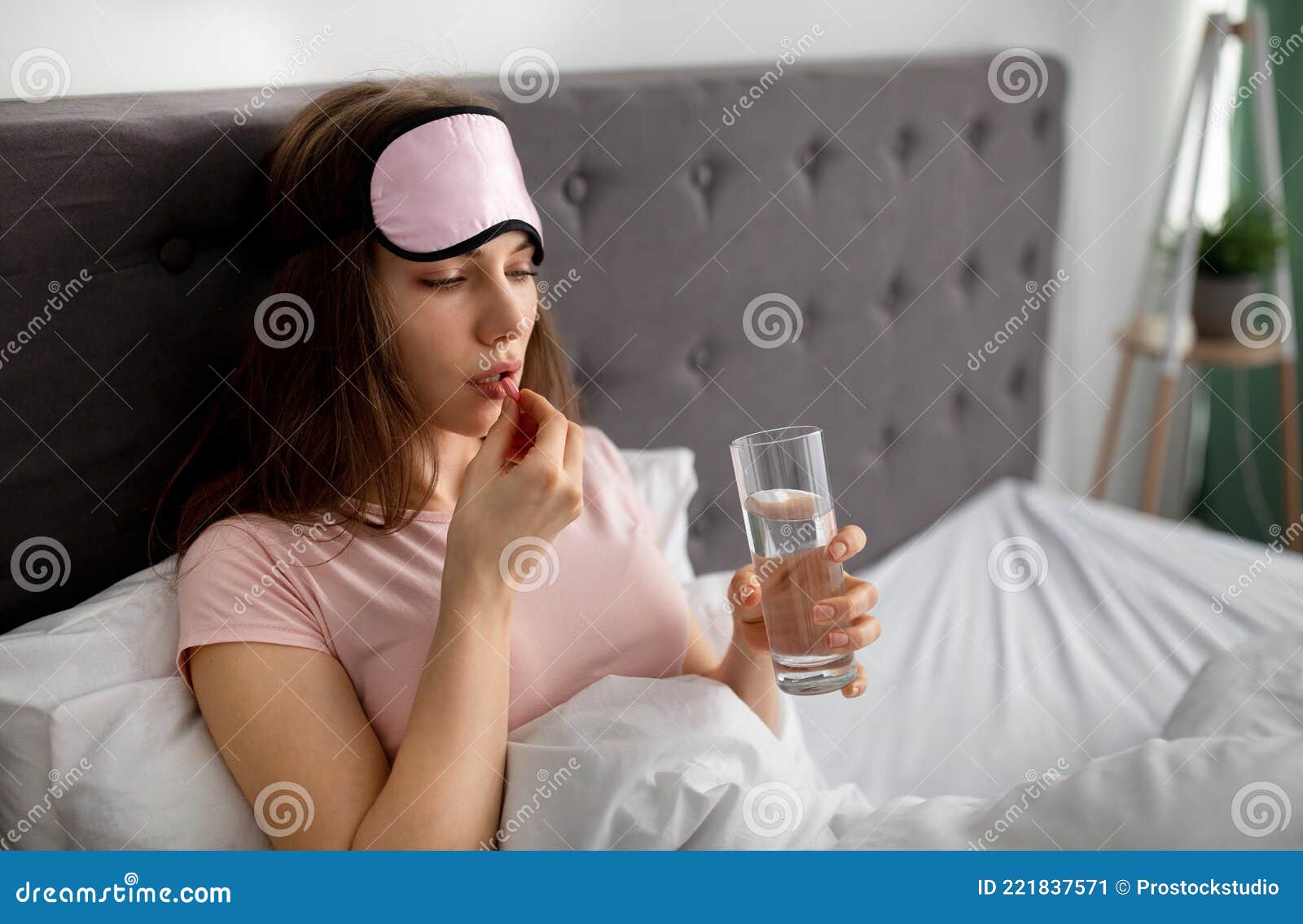 Sleepy Young Woman With Glass Of Water Taking Pill In Bed At Home Copy