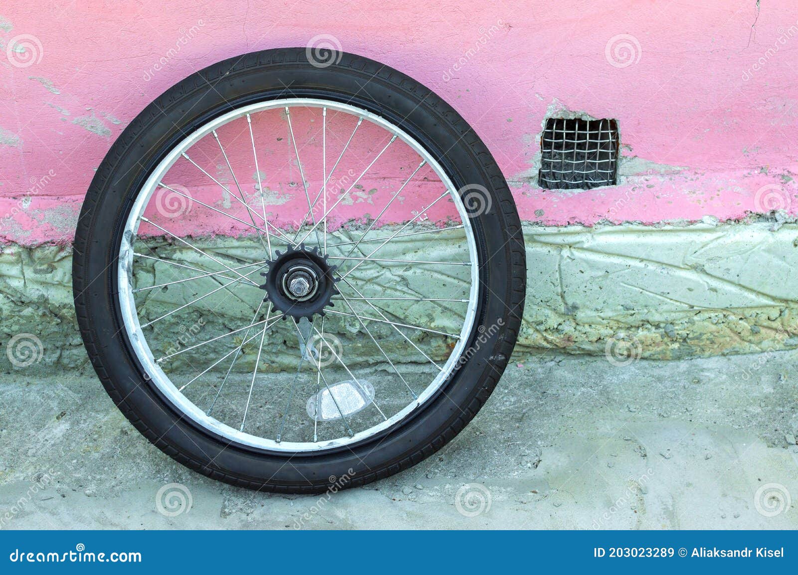 A Small Bicycle Wheel Rests on the Concrete Pink Wall of the House ...