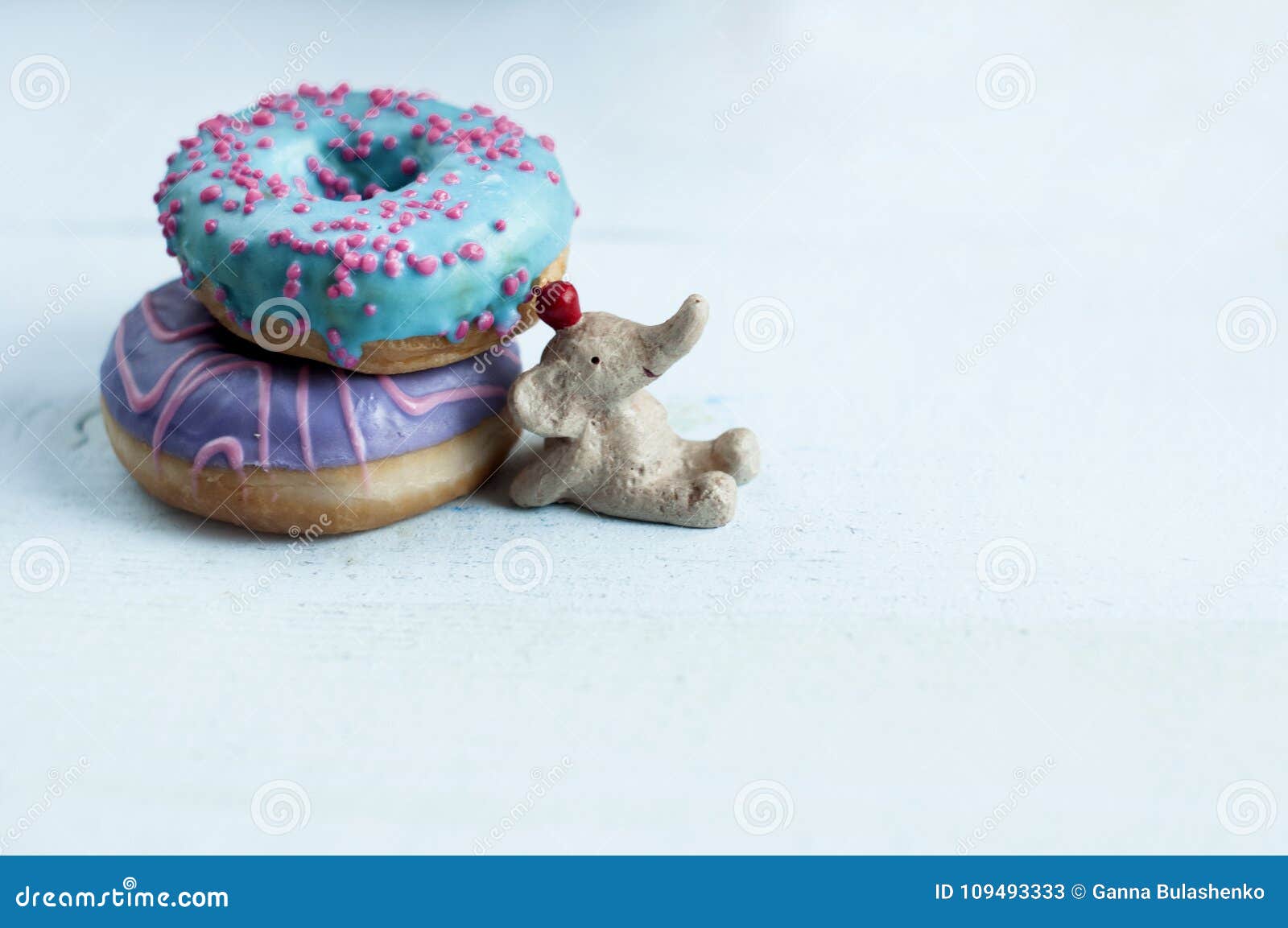A Small Elephant Figurine Propped Up with Two Different Colored Donuts ...