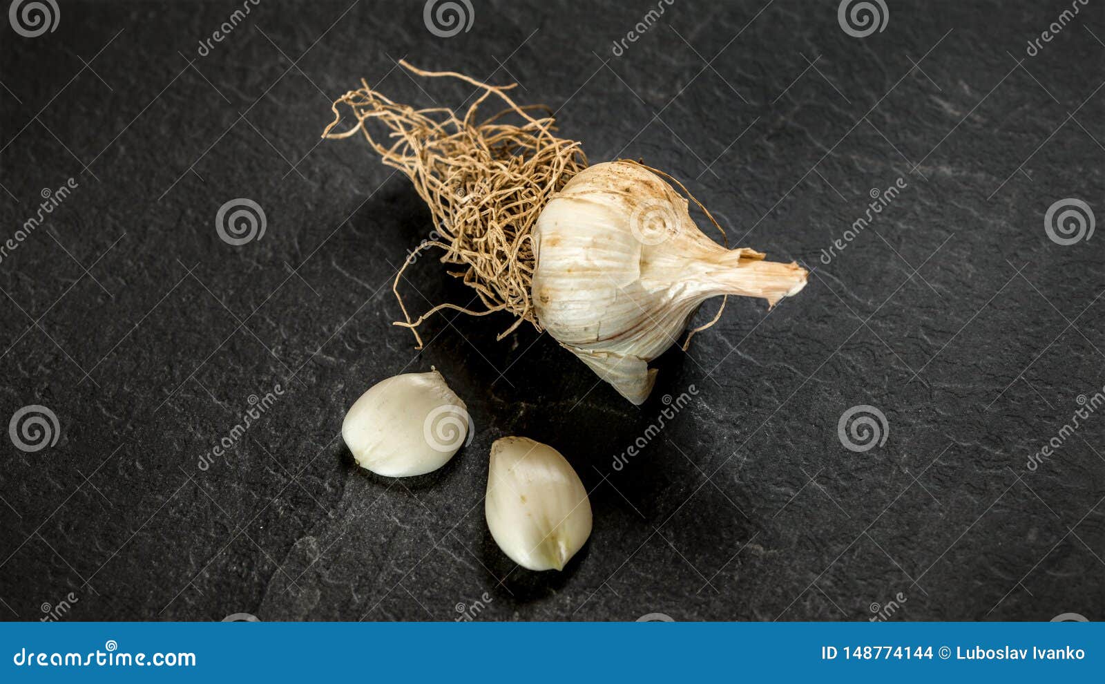 Small Garlic Bulb with Roots, Two Cloves Next on Black Working Board ...