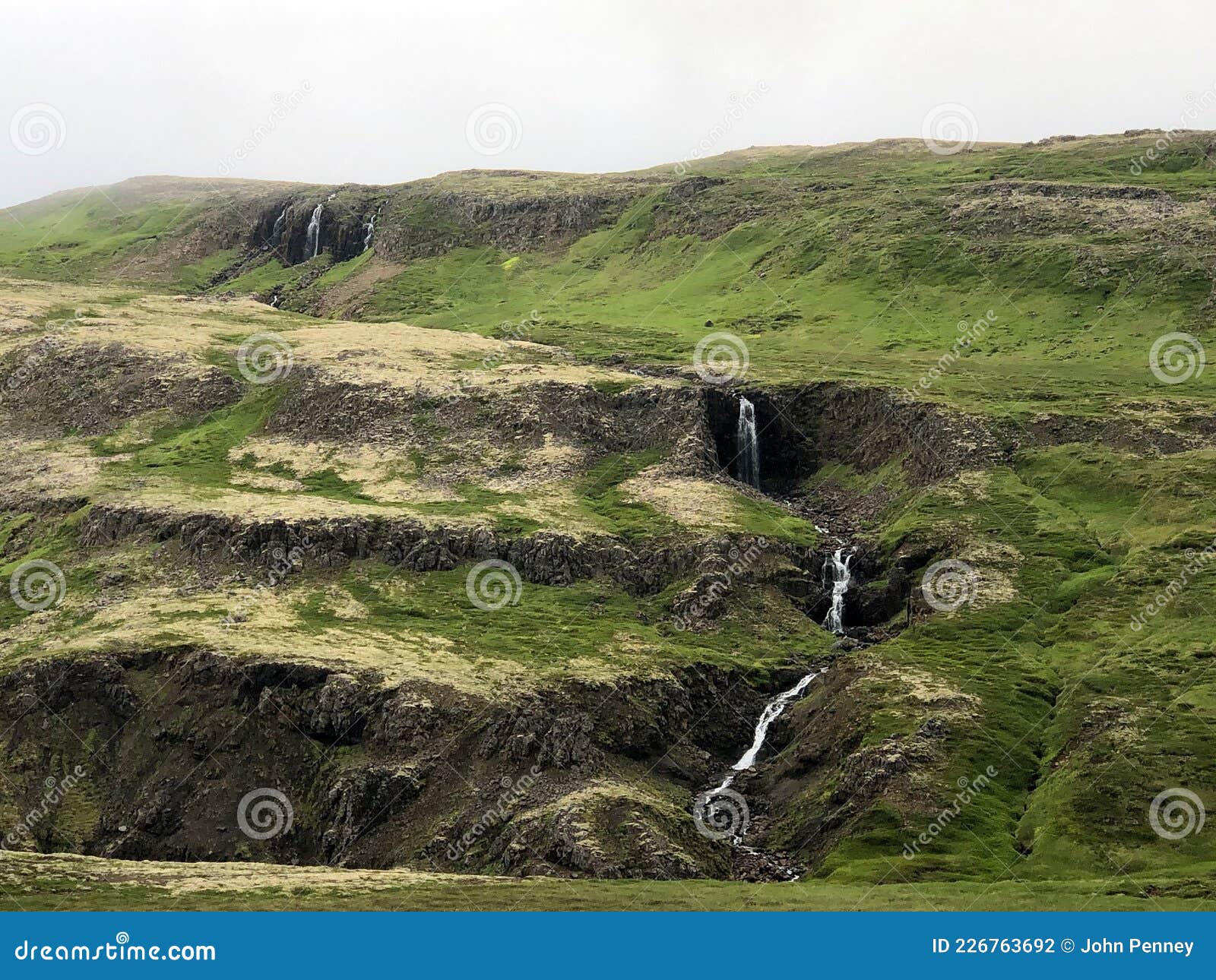 A Small Long Waterfall with Four Separate Sections Drops Down a Green ...
