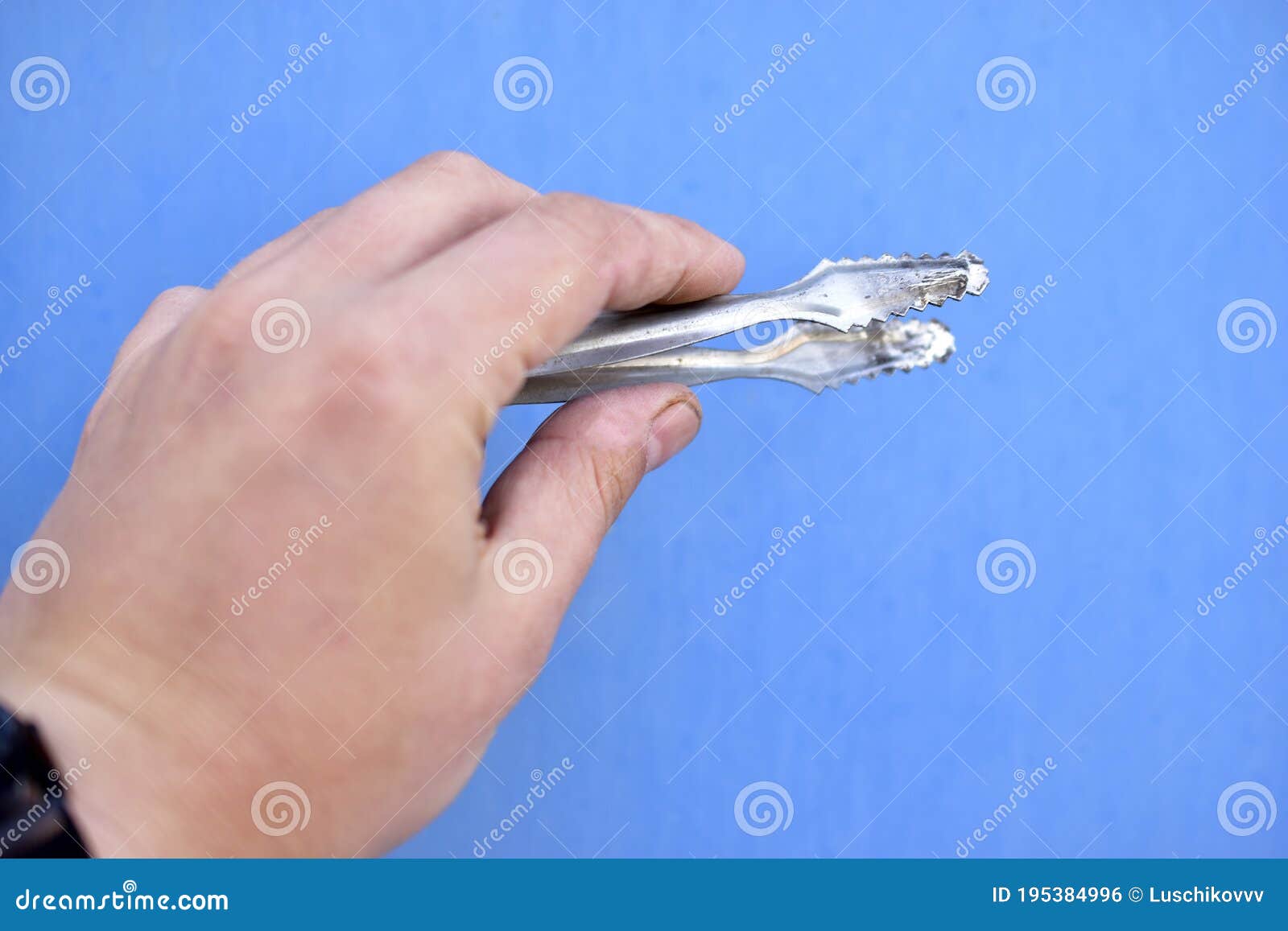 Small Metal Tongs in Hand on a Blue Background Stock Photo - Image of ...