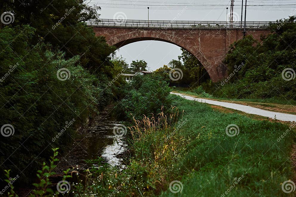 A Small River Parallel To the Road Leads To the Arch of the Road Bridge ...