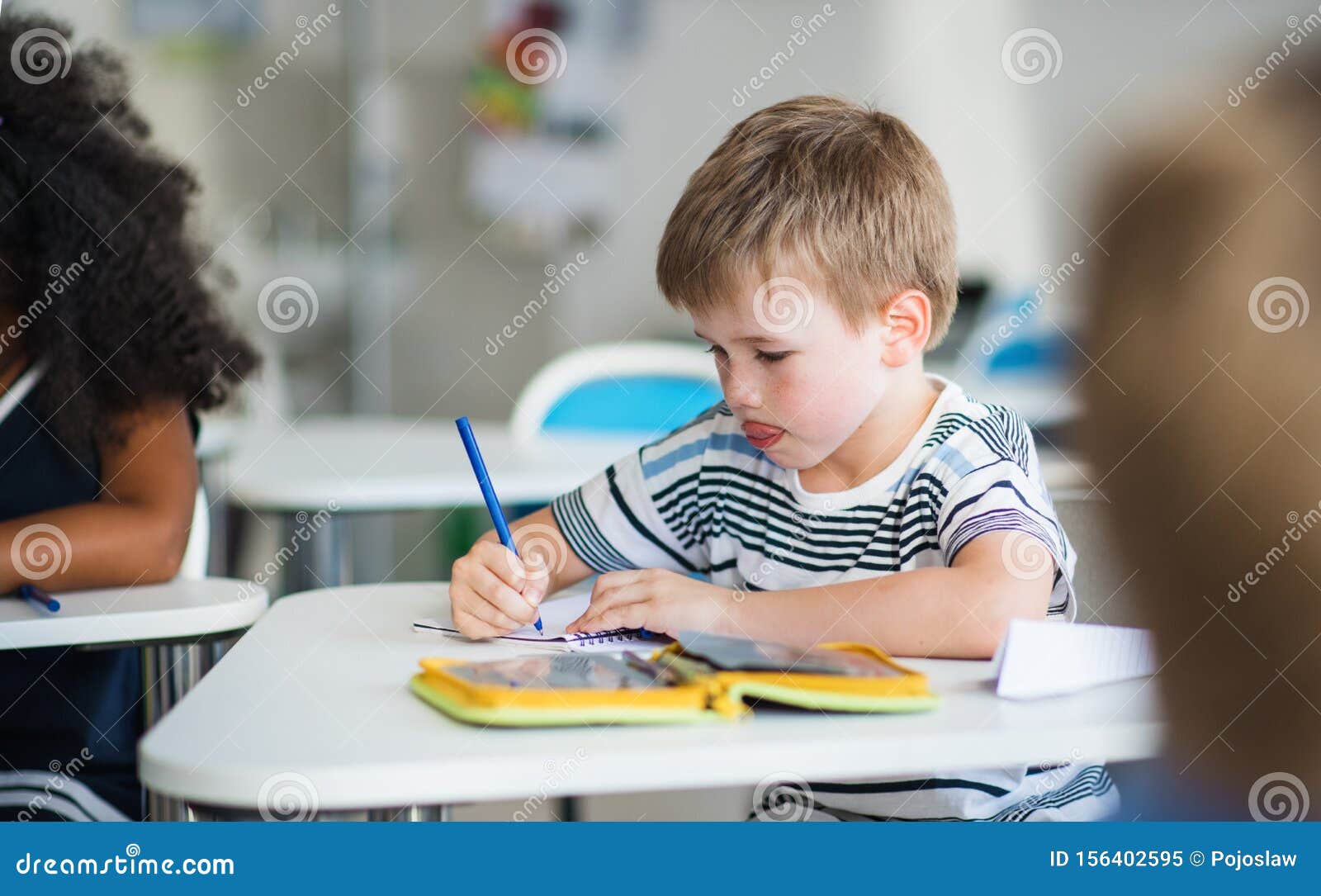 A Small School Boy Sitting at the Desk in Classroom, Writing. Stock ...