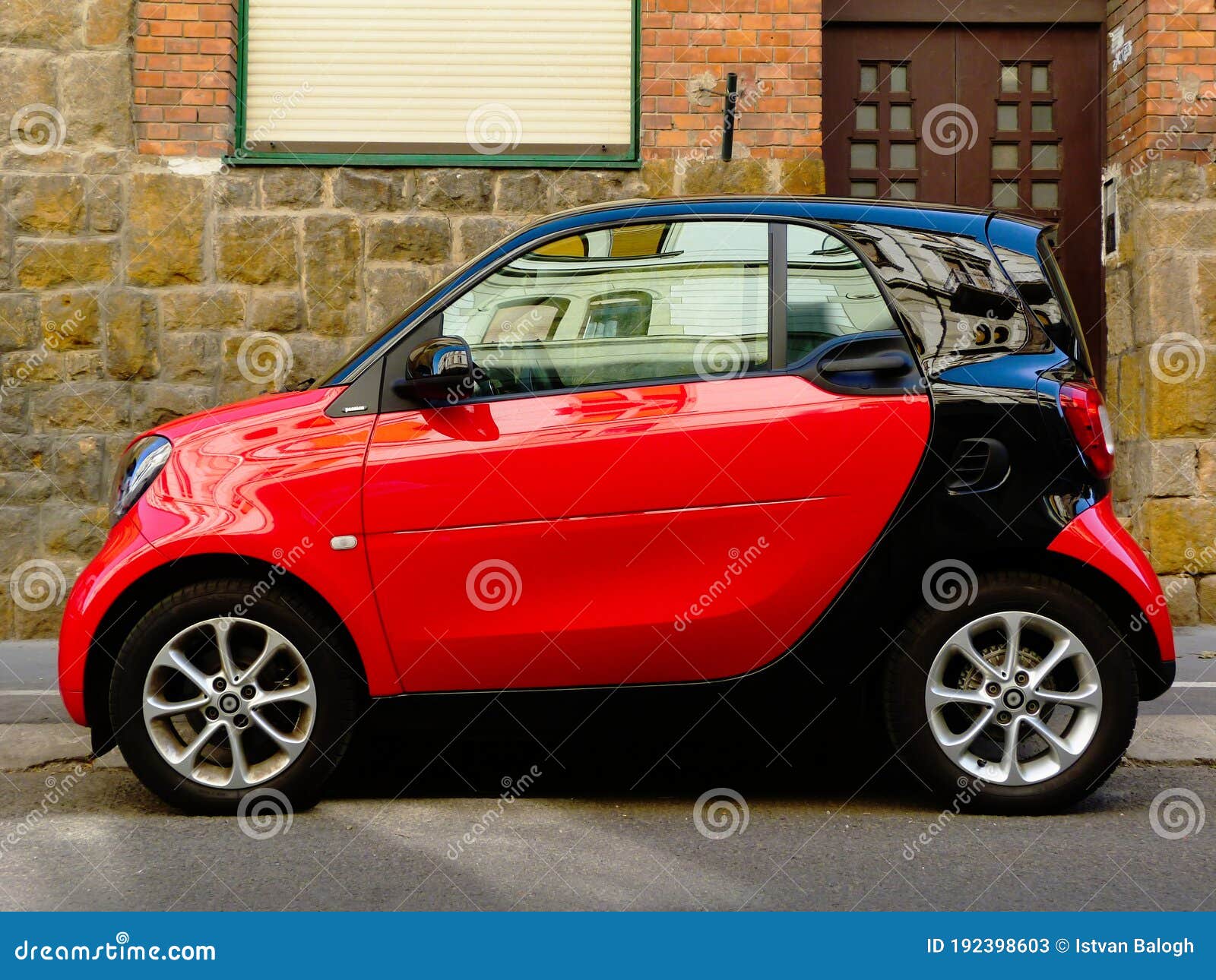 Small Two Seater Red And Black Modern Compact Town Car In Side View In Old Urban Setting Stock