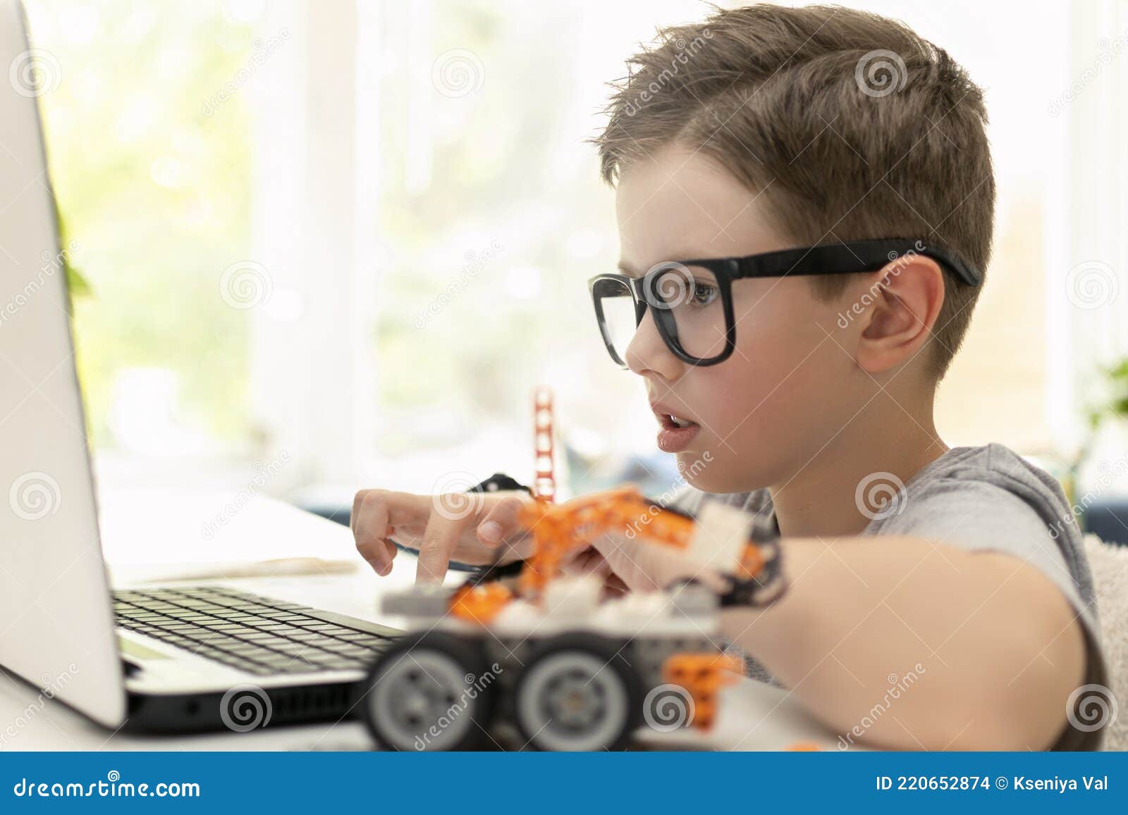 A Smart Boy Builds a Robot Car Using a Laptop Near the Window at Home ...